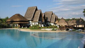 Um resort com uma grande piscina, construções com telhados de palha e um jardim tropical.