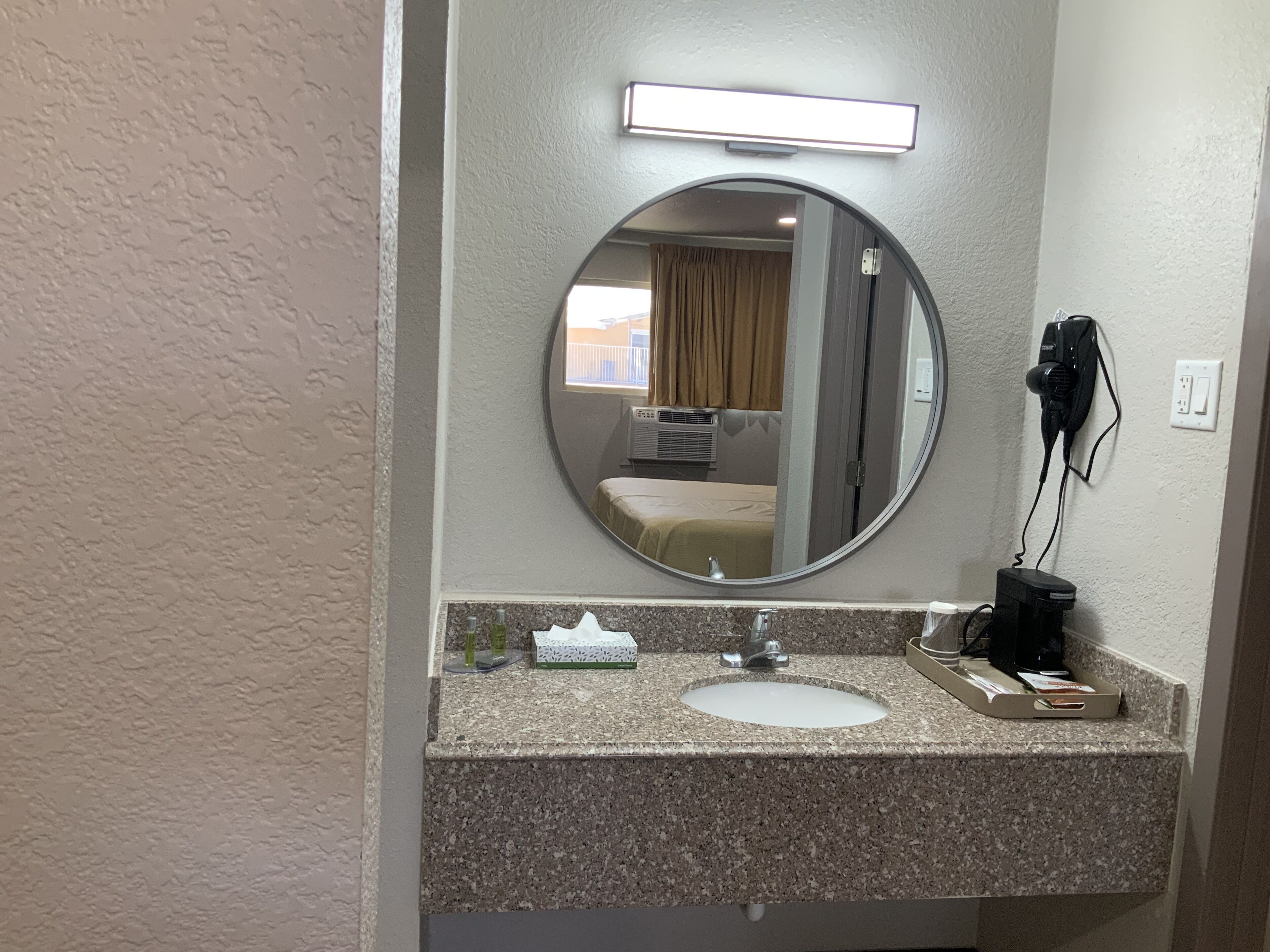 Um banheiro de hotel com espelho redondo, pia e secador de cabelo na parede.