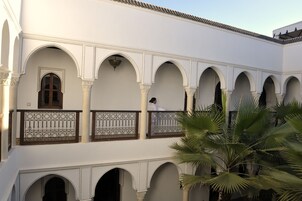 Um pátio com paredes brancas, várias arcadas e uma varanda com grade de ferro forjado.