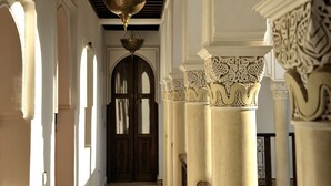 Um corredor interno com colunas ornamentadas e uma porta de madeira.