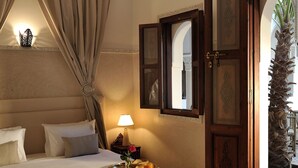 Quarto de hotel com uma cama grande, uma mesa de cabeceira com abajur, um tabuleiro com itens de café da manhã e vista para o exterior através de uma porta aberta.