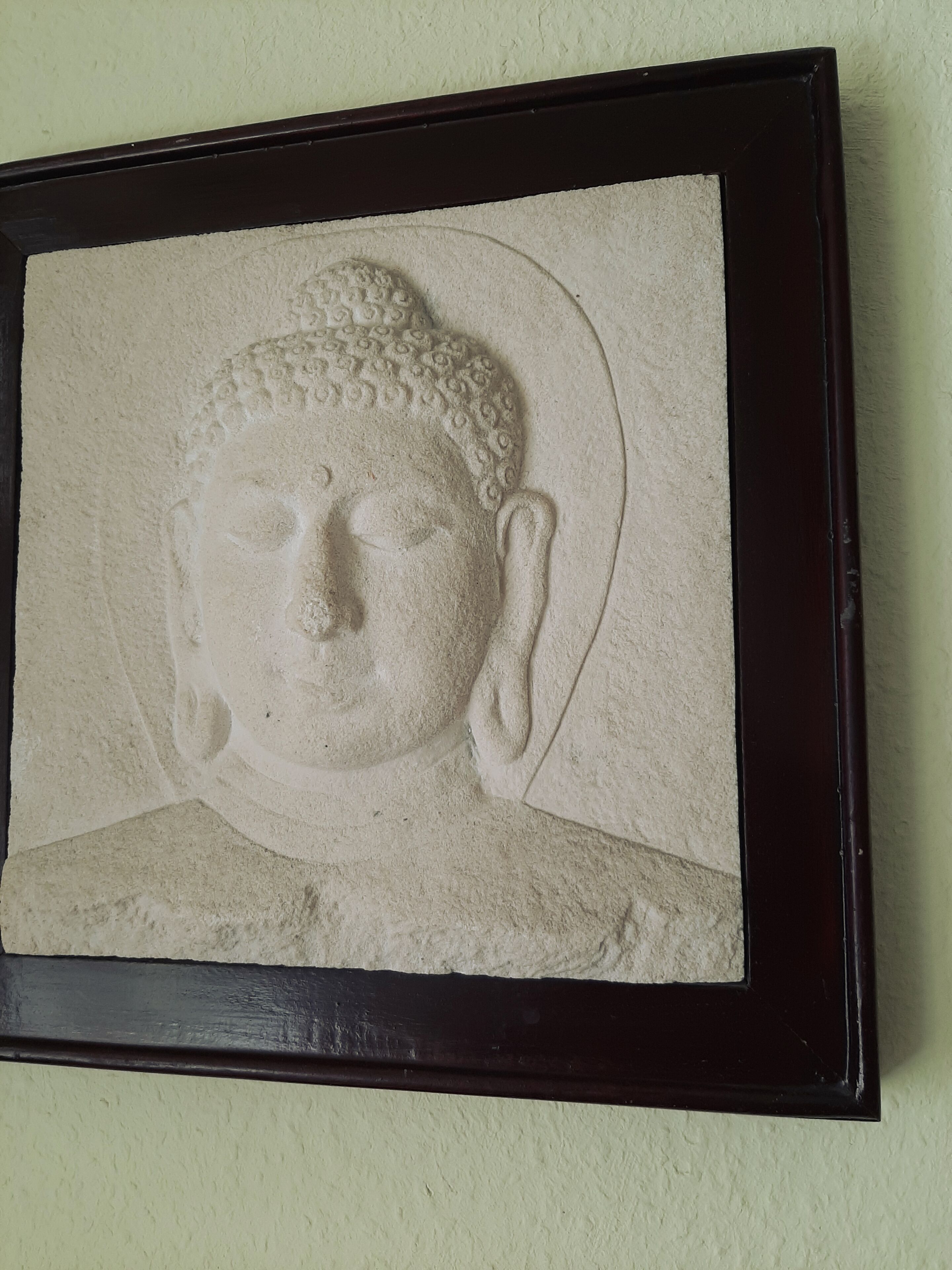 Escultura de areia da cabeça de Buda emoldurada em tom escuro.
