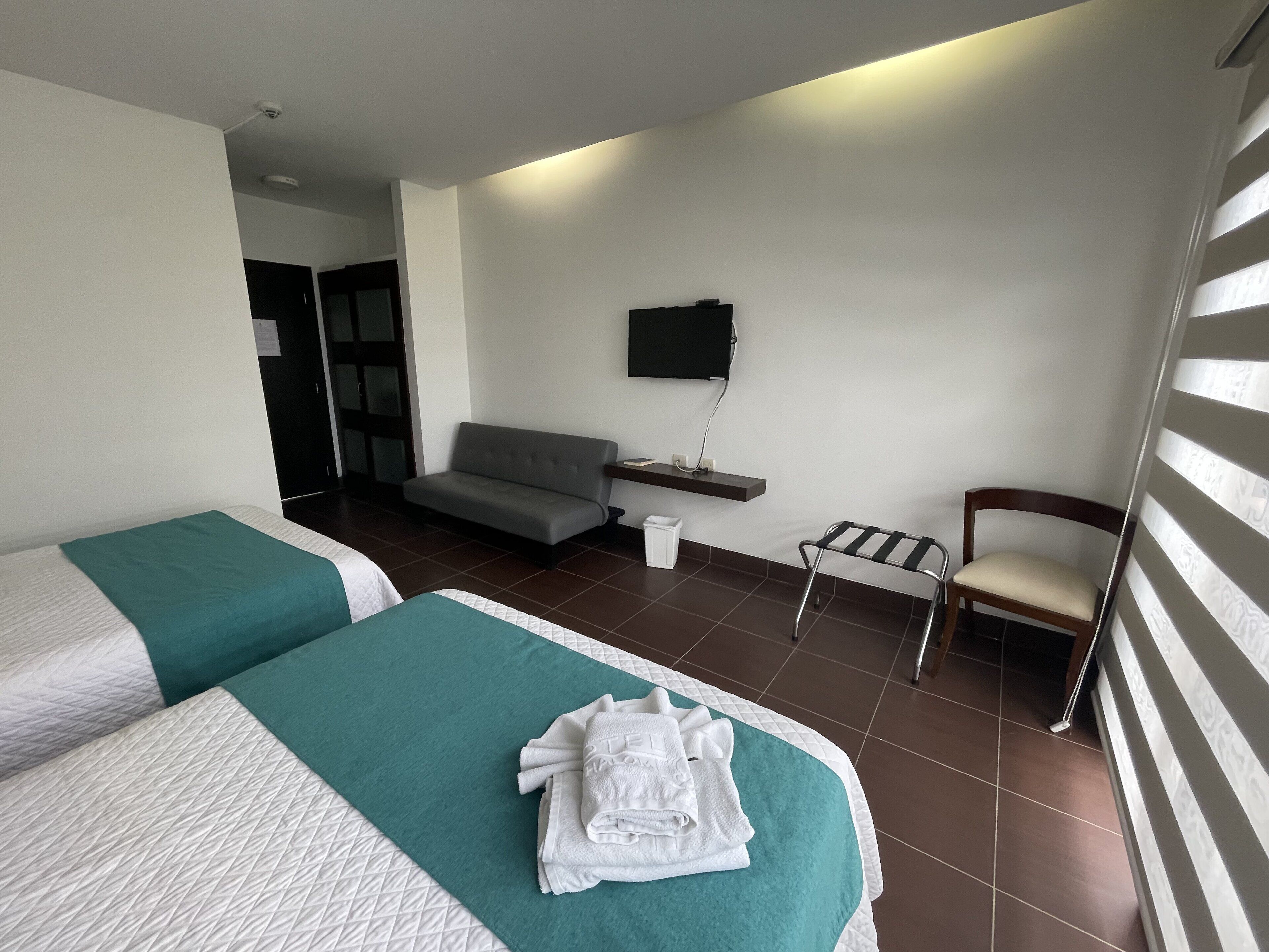 Quarto de hotel com duas camas, um sofá, uma televisão e uma cadeira.