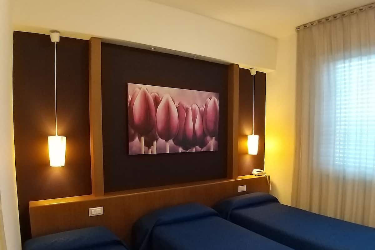 Quarto de hotel com duas camas, uma grande obra de arte floral na parede e duas luminárias de parede.