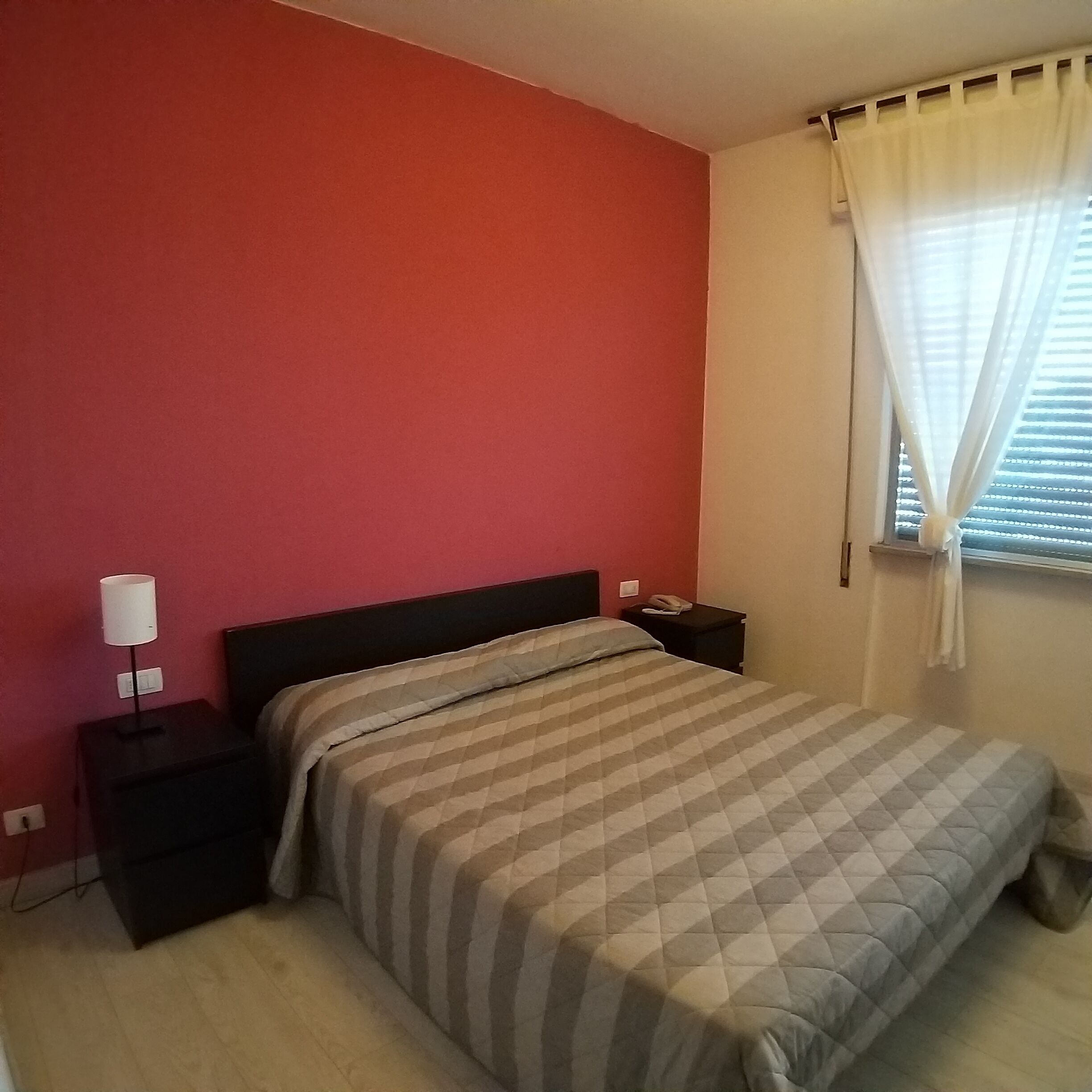 Quarto com uma cama, mesa de cabeceira, luminária e janela com cortinas.