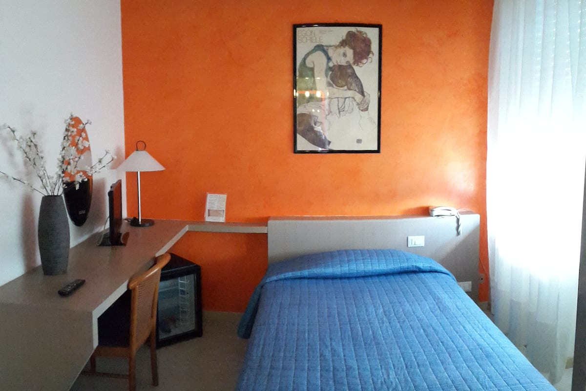 Quarto com cama, escrivaninha, cadeira, abajur e quadro na parede.