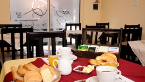 Mesa posta para o café da manhã com pão, croissants, café e suco.