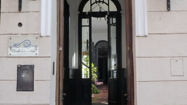 Uma entrada arqueada com uma porta de madeira, duas lanternas fixadas na parede e uma placa sobre a porta.