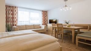 Quarto de hotel moderno com uma cama grande, um sofá, uma mesa de jantar com cadeiras, uma televisão e uma planta.