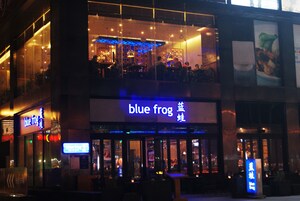 Um restaurante chamado 'Blue Frog' com mesas ao ar livre e vista para a cidade à noite.