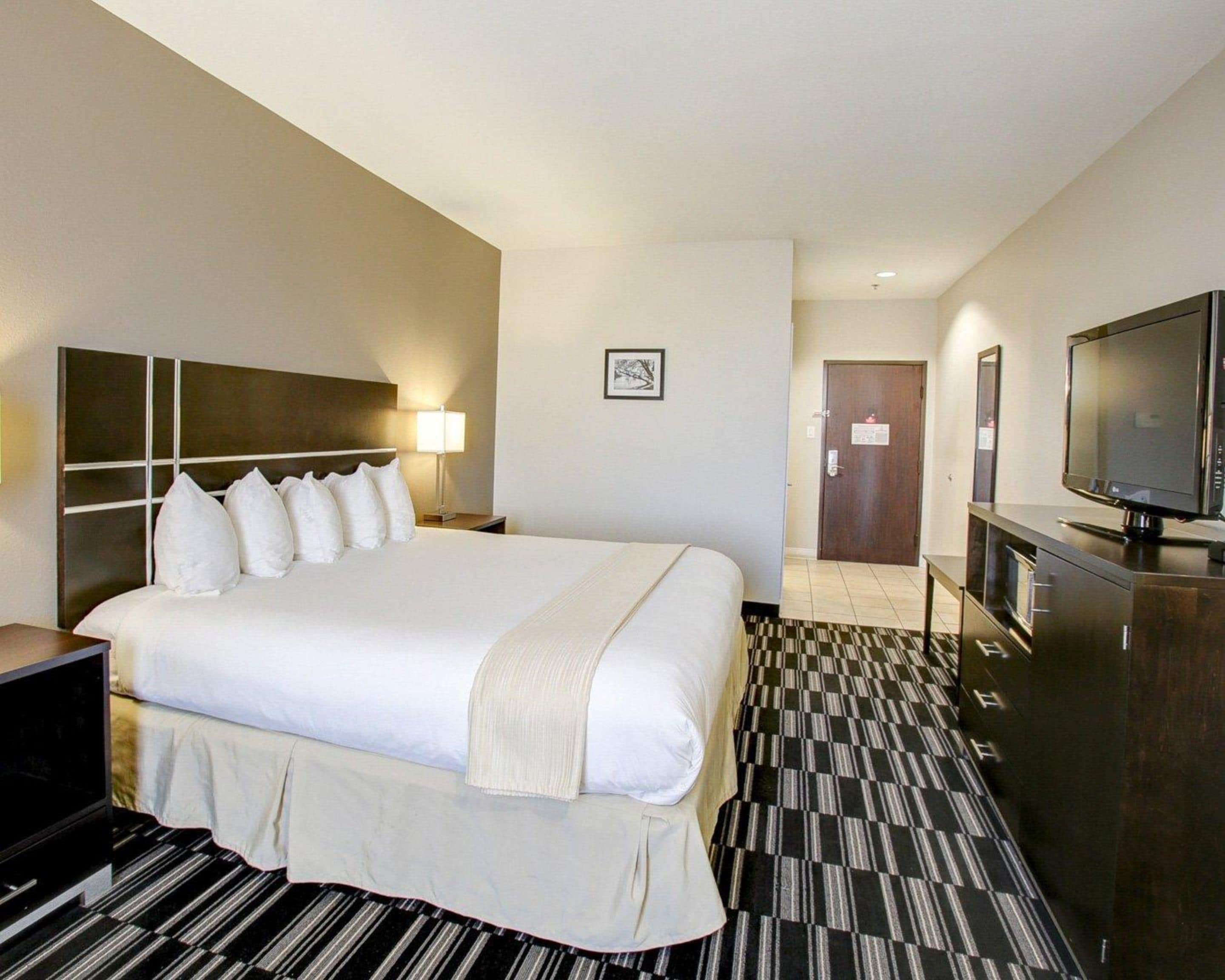 Quarto de hotel com uma cama grande, televisão, escrivaninha e porta.