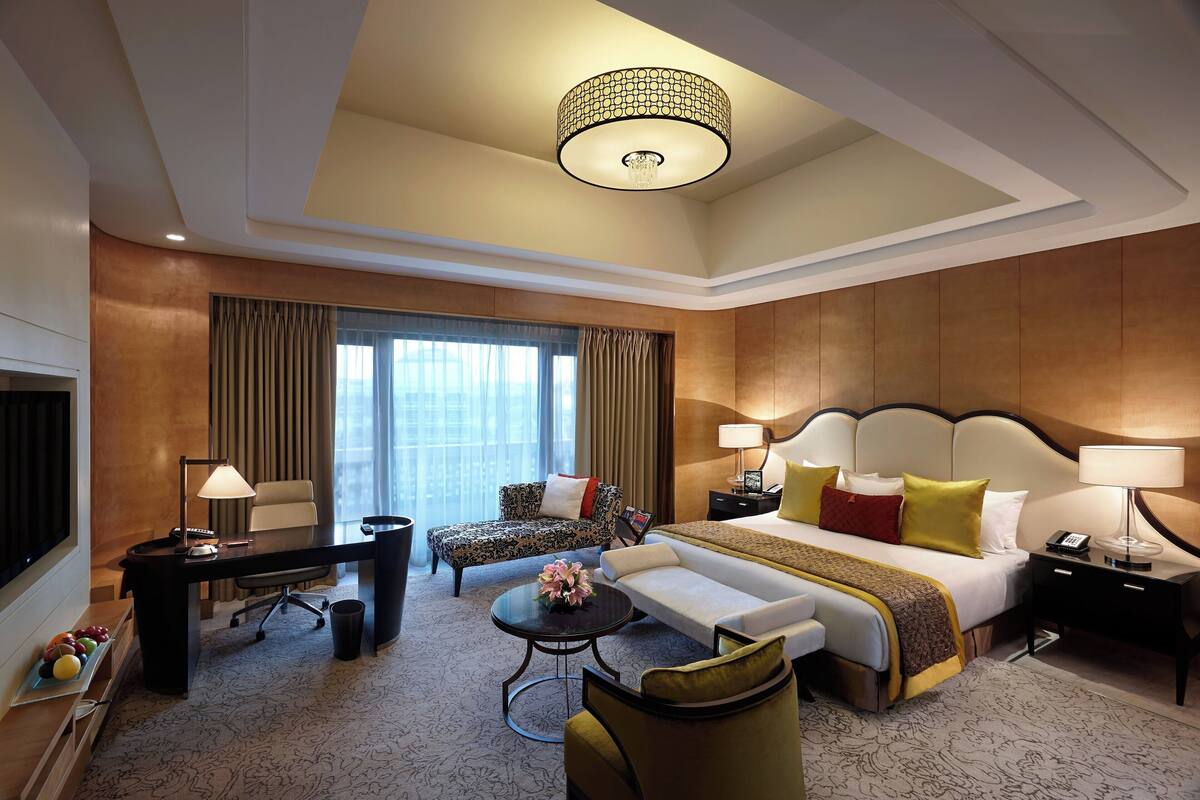 Quarto de hotel com uma cama grande, uma escrivaninha, um sofá, uma cadeira, uma mesa pequena e uma televisão.