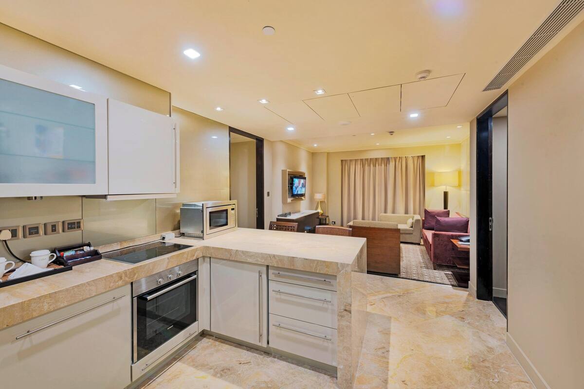 Quarto de hotel moderno com cozinha, sala de estar com sofá e televisão, e uma área de refeições separada.