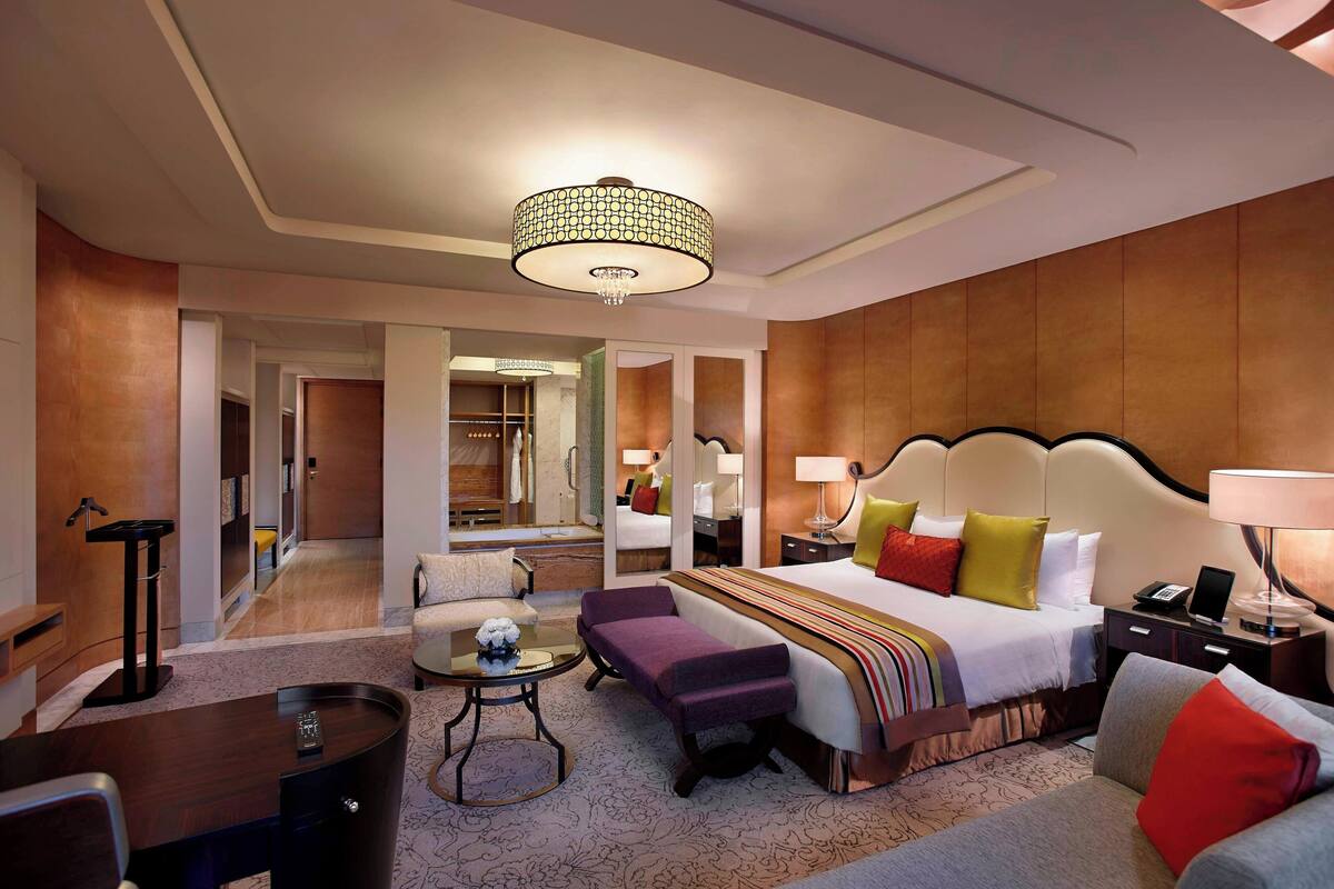Quarto de hotel com uma cama grande, uma escrivaninha, uma cadeira, um sofá e um abajur.