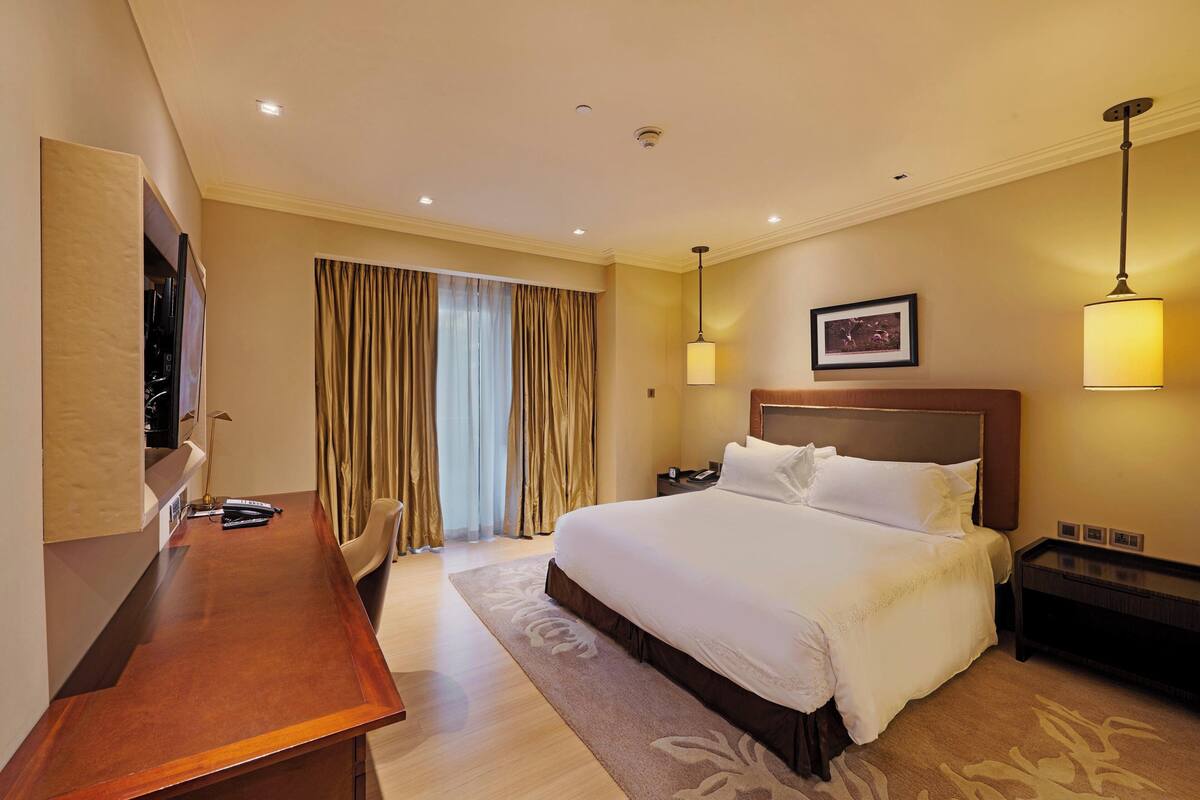 Quarto de hotel com uma cama grande, uma escrivaninha, uma cadeira, uma TV e um quadro na parede.