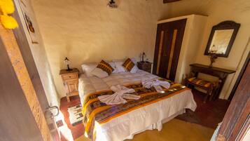 Quarto com uma cama grande, mesa de cabeceira de madeira, espelho e um banco de madeira.