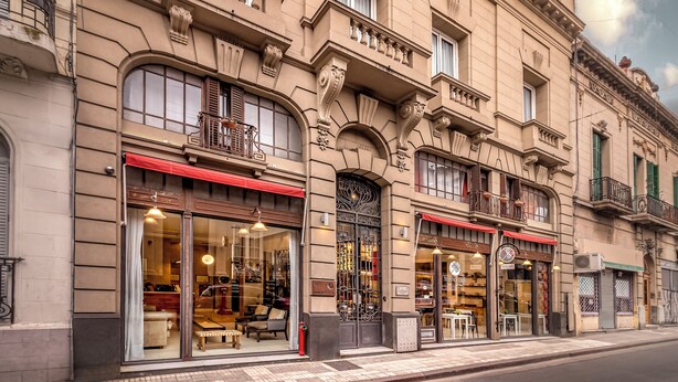 Um edifício histórico com detalhes arquitetônicos elaborados, grandes vitrines de vidro e um toldo vermelho.