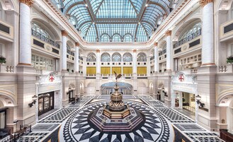 Um amplo hall de hotel com uma fonte central, tetos altos e piso de mármore detalhado.