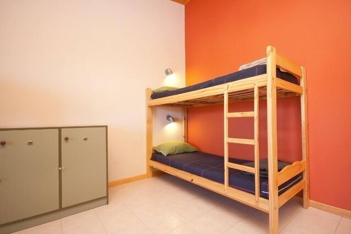 Uma cama de beliche com escada, uma escrivaninha com gavetas e um armário em um quarto com paredes laranja.