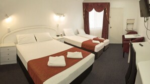 Quarto de hotel com duas camas, uma escrivaninha, uma cadeira, uma televisão e uma porta.