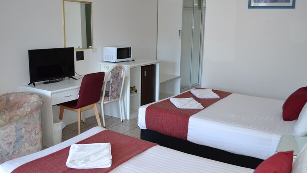 Quarto de hotel com duas camas, uma mesa com computador, uma cadeira e um micro-ondas.
