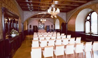 Interior com fileiras de cadeiras brancas dispostas para um evento, tetos em arco e um candelabro.