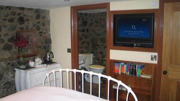 Quarto com cama, televisão na parede, mesa de cabeceira com livros e parede de pedra.