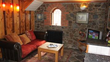 Uma sala de estar aconchegante com um sofá de madeira, uma mesa de centro e uma parede de pedra com uma janela.