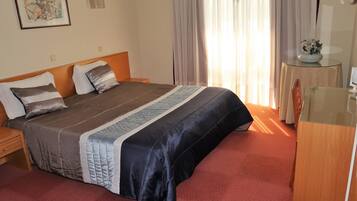 Quarto de hotel com uma cama grande, uma mesa de cabeceira de madeira, uma pequena mesa com um vaso e um espelho.