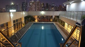 Piscina no terraço com vista para o horizonte urbano à noite.