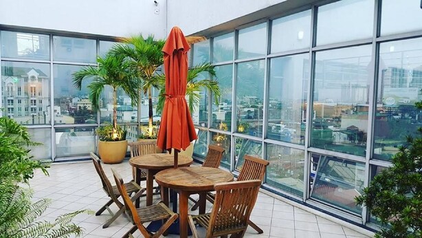 Uma varanda com mesa e cadeiras de madeira, plantas em vasos e um guarda-sol vermelho.