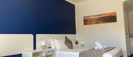 Quarto de hotel com duas camas, uma mesa de cabeceira, uma mesinha e um quadro na parede.