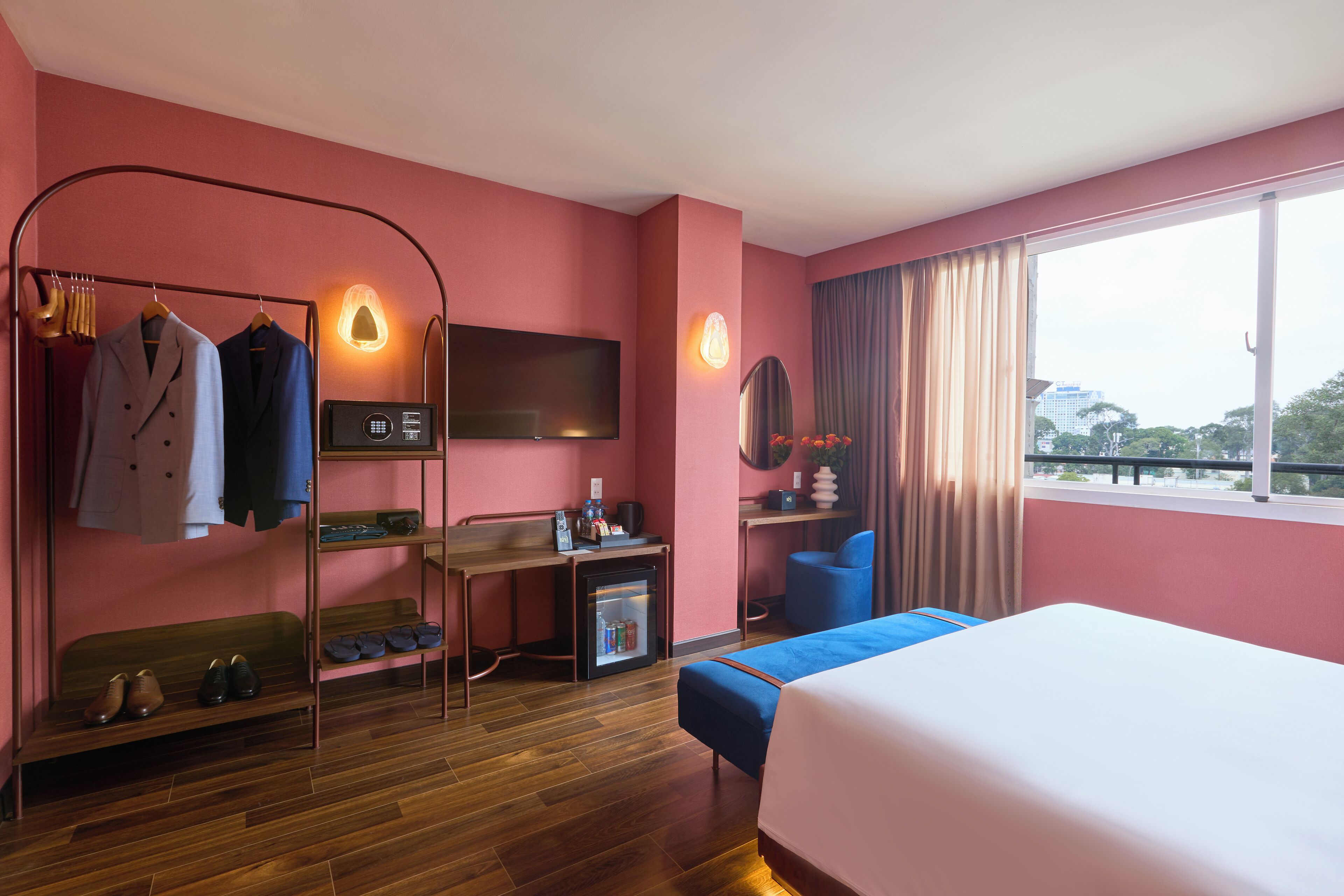 Quarto de hotel com cama, escrivaninha com computador, televisão, guarda-roupa e janela com vista.