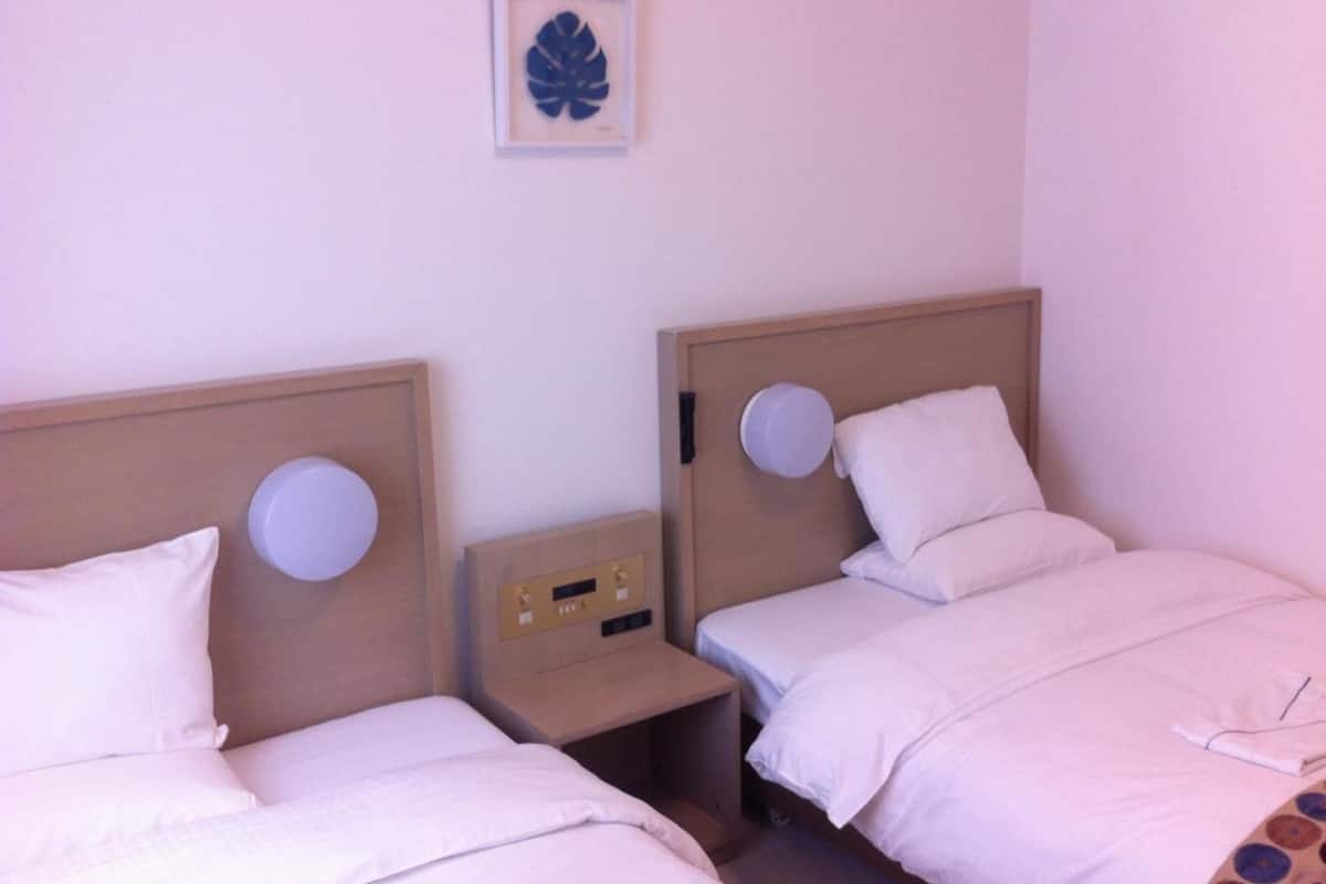Quarto de hotel com duas camas de solteiro, cada uma com cabeceira de madeira e mesa de cabeceira com abajur.