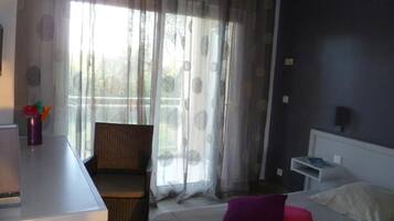 Quarto de hotel com cama, uma cadeira, escrivaninha e janela com cortinas.