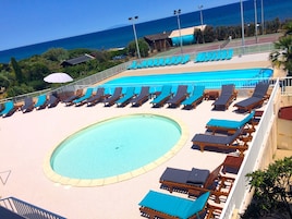 Uma área de piscina com espreguiçadeiras e uma piscina central, cercada por uma grade e com vista para o oceano.