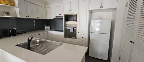 Uma cozinha moderna com armários brancos, eletrodomésticos de aço inoxidável e bancada preta.