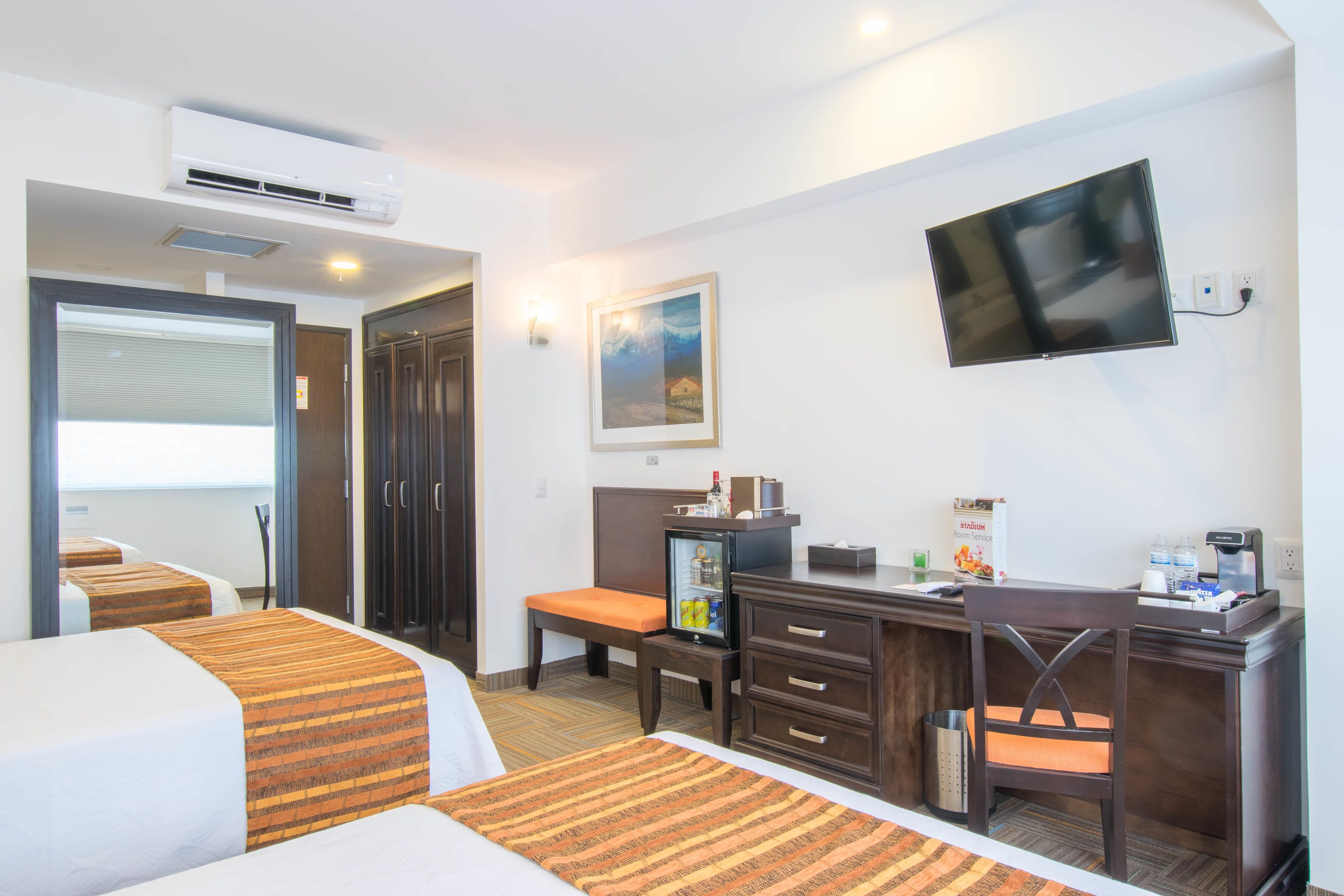 Quarto de hotel com duas camas, uma escrivaninha com computador, televisão e minibar.