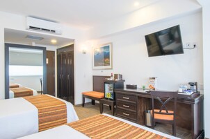 Quarto de hotel com duas camas, uma escrivaninha com computador, televisão e minibar.