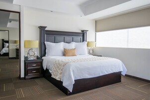 Quarto de hotel com uma cama grande, duas mesas de cabeceira, um espelho e uma janela com persianas.