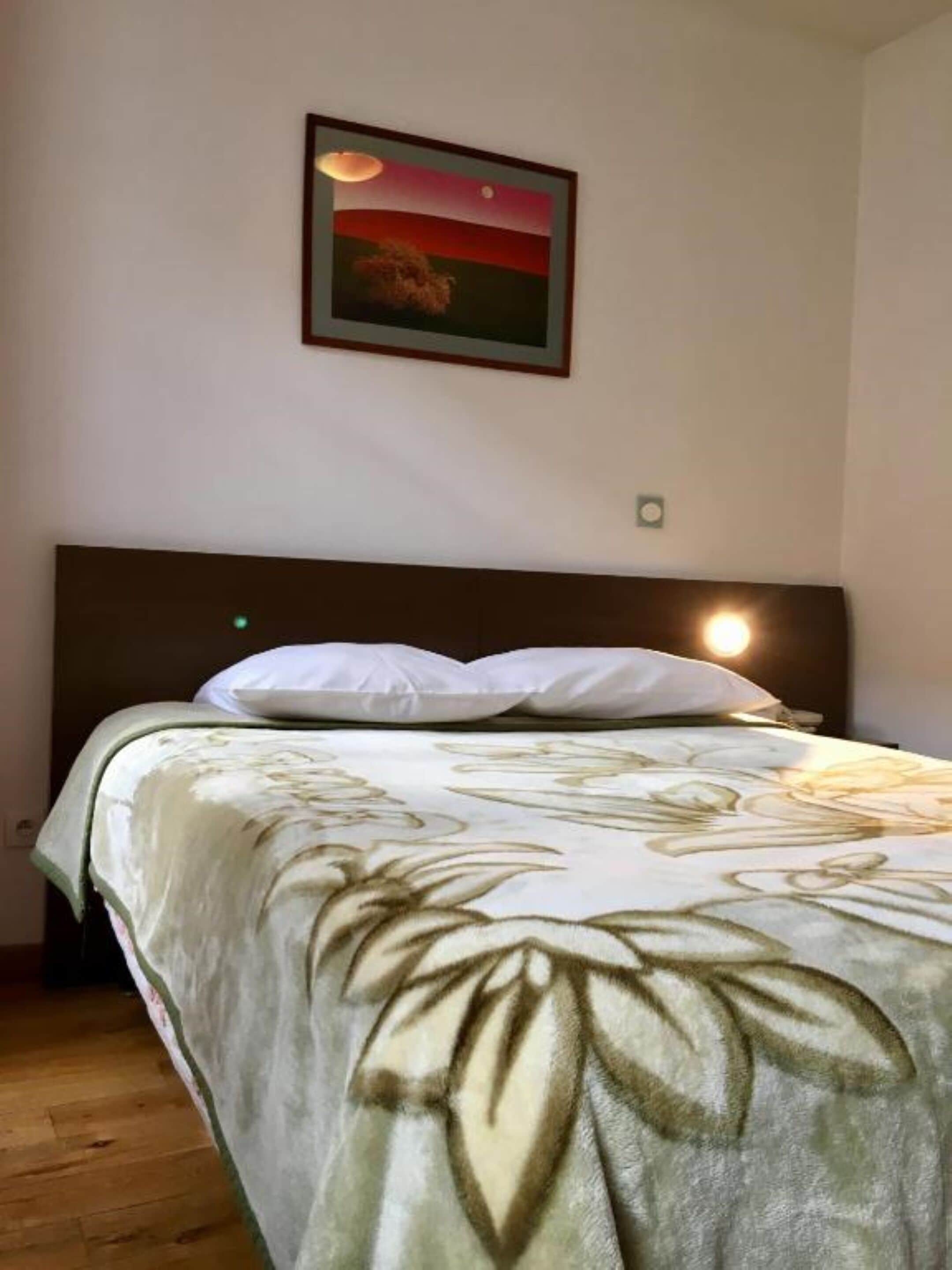 Uma cama bem arrumada com colcha florida, um quadro na parede e um abajur.