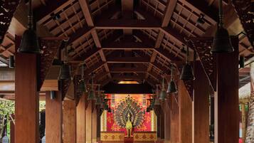 Uma galeria coberta com piso estampado, pilares de madeira e sinos pendurados.
