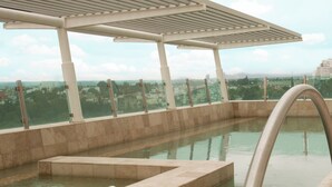 Piscina no terraço com vista clara da cidade, escadas descendo até a piscina e área coberta com corrimão.