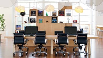 Um escritório moderno com uma longa mesa de madeira, quatro cadeiras de escritório pretas e dois monitores de computador.