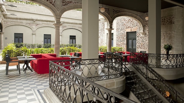 Um café ao ar livre com assentos vermelhos, paredes de pedra e chão xadrez.