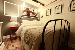 Quarto com cama, mesa de cabeceira, luminária e quadros na parede.