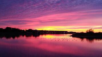Um lago tranquilo ao pôr do sol, com o reflexo do céu e a silhueta de uma cidade ao longe.
