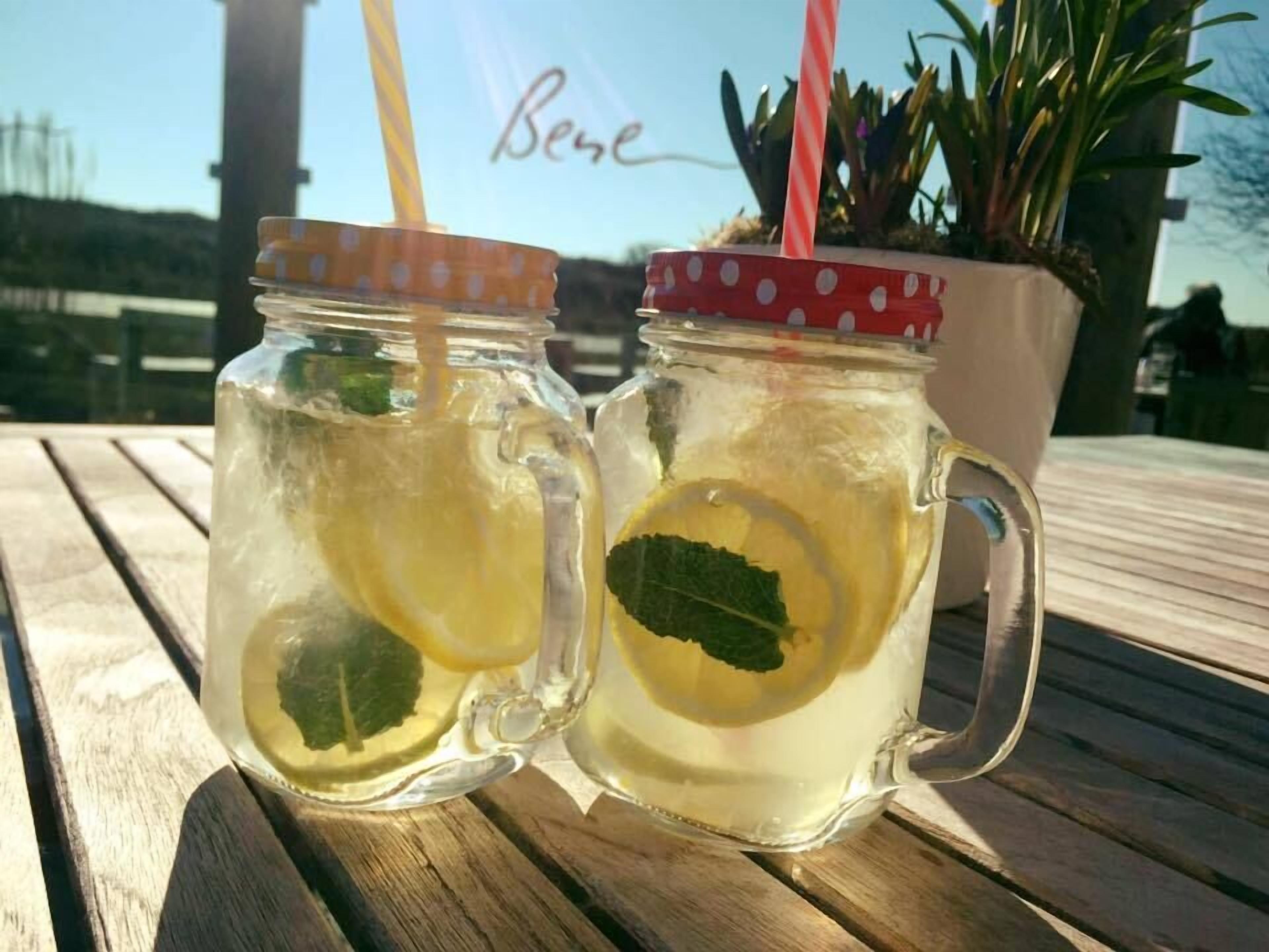 Dois potes de vidro com canudos e rodelas de limão sobre uma mesa de madeira.