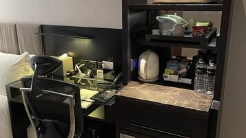 Quarto de hotel pequeno com escrivaninha, cadeira e minibar.