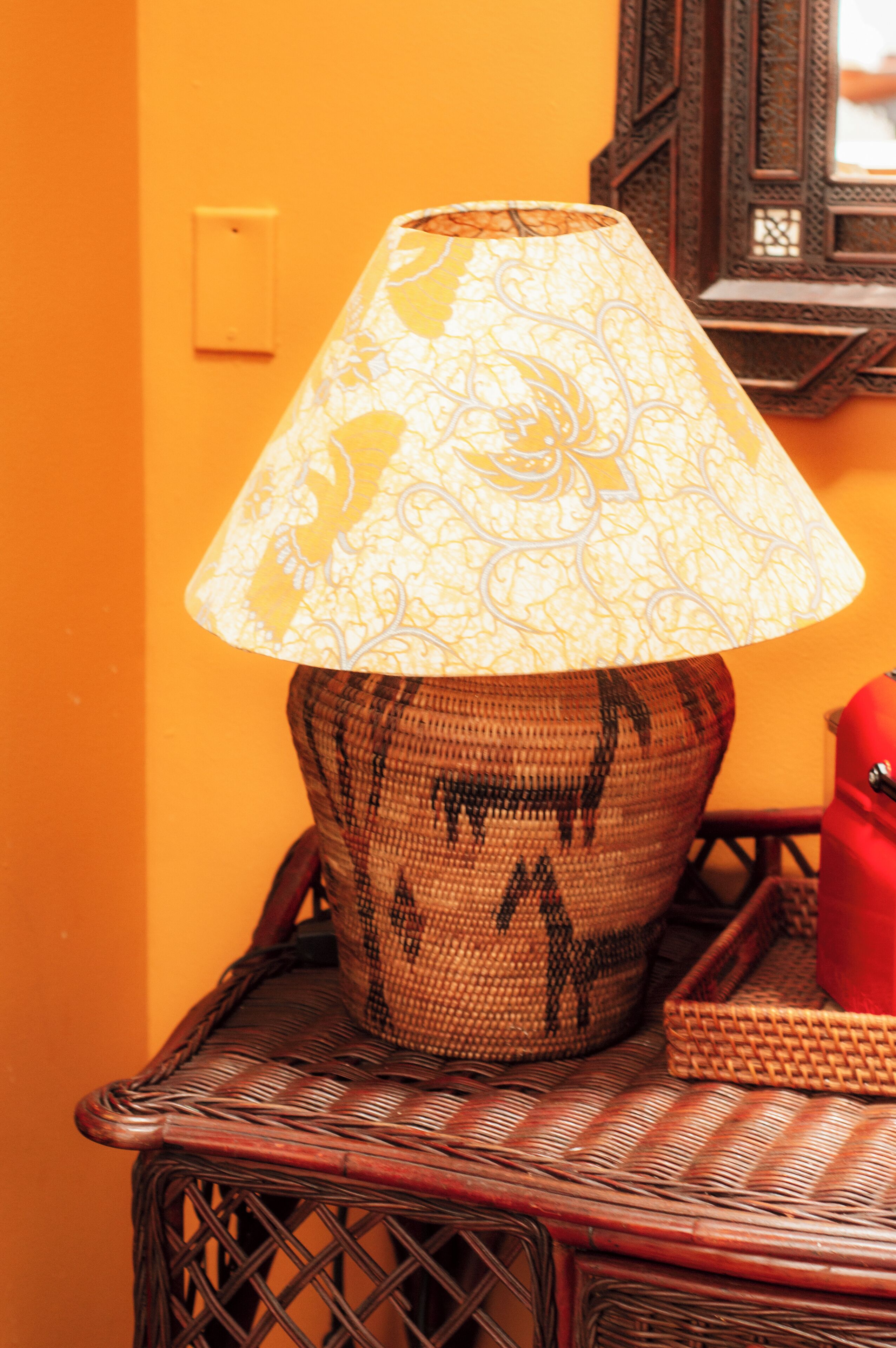 Luminária de vime com cúpula estampada sobre uma cadeira de vime.